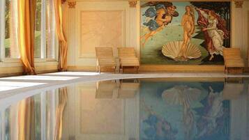 Quarto com piscina grande, mural com figuras clássicas e área de estar com cadeiras.