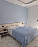 Quarto de hotel com cama, mesa de cabeceira com abajur, telefone e painel de controle fixado na parede.