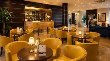 Um saguão de hotel com assentos amarelos, um espaço de bar e uma mesa de recepção.