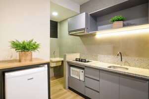 Uma cozinha compacta com micro-ondas integrado, pia e pequeno frigorífico.