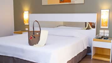 Cama bem arrumada com edredom branco, uma bolsa marrom sobre a cama e uma mesa de cabeceira com abajur e telefone.