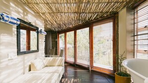 Um espaço de spa com um deck de madeira, uma banheira branca e um sofá com almofadas.