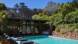 Área de piscina com espreguiçadeiras, um muro de pedra e montanhas ao fundo.