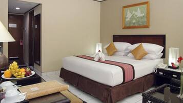 Quarto de hotel com cama arrumada, cesta de frutas, mesa de cabeceira com abajur e um quadro na parede.