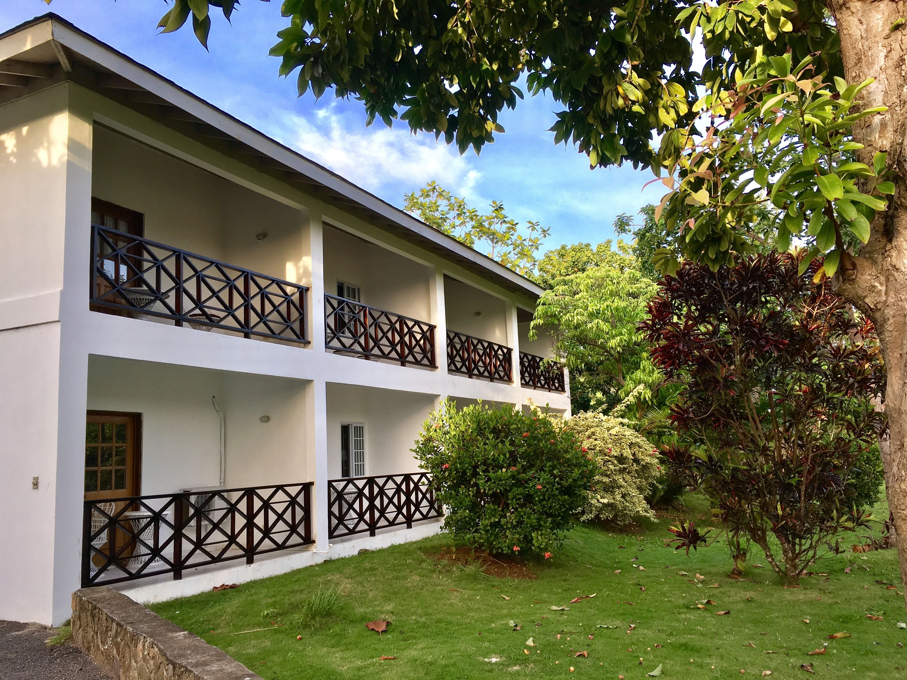 Um edifício de dois andares com varandas, gramado e árvores ao redor.