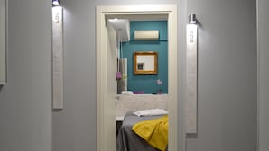 Um corredor estreito que dá para um banheiro com uma cama, um espelho e um porta-toalhas.