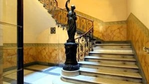 Uma escadaria com uma estátua no topo, paredes de mármore e piso estampado.