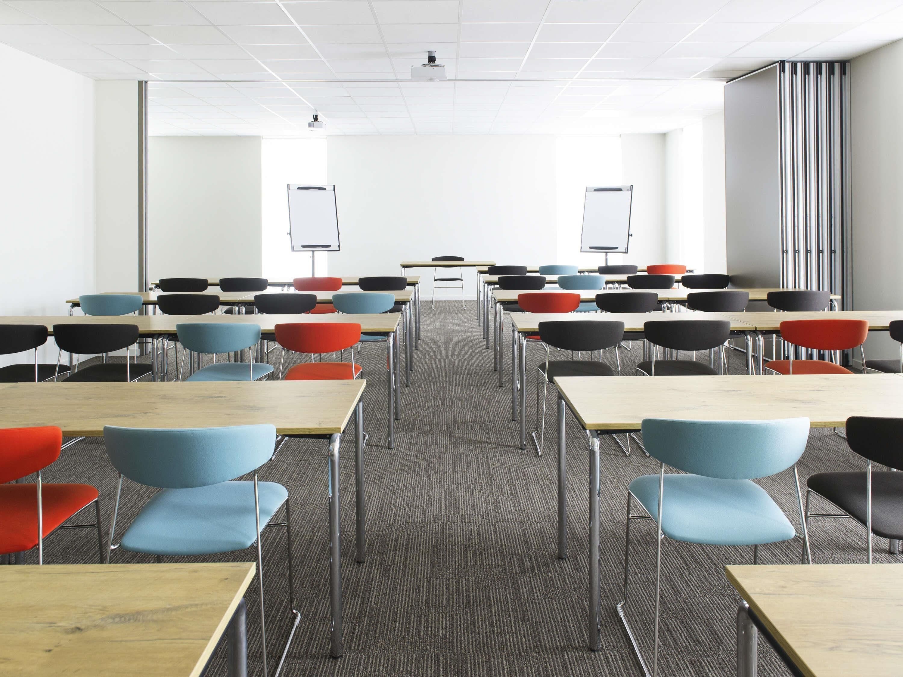 Uma sala de aula com fileiras de mesas e cadeiras, um projetor e uma lousa.