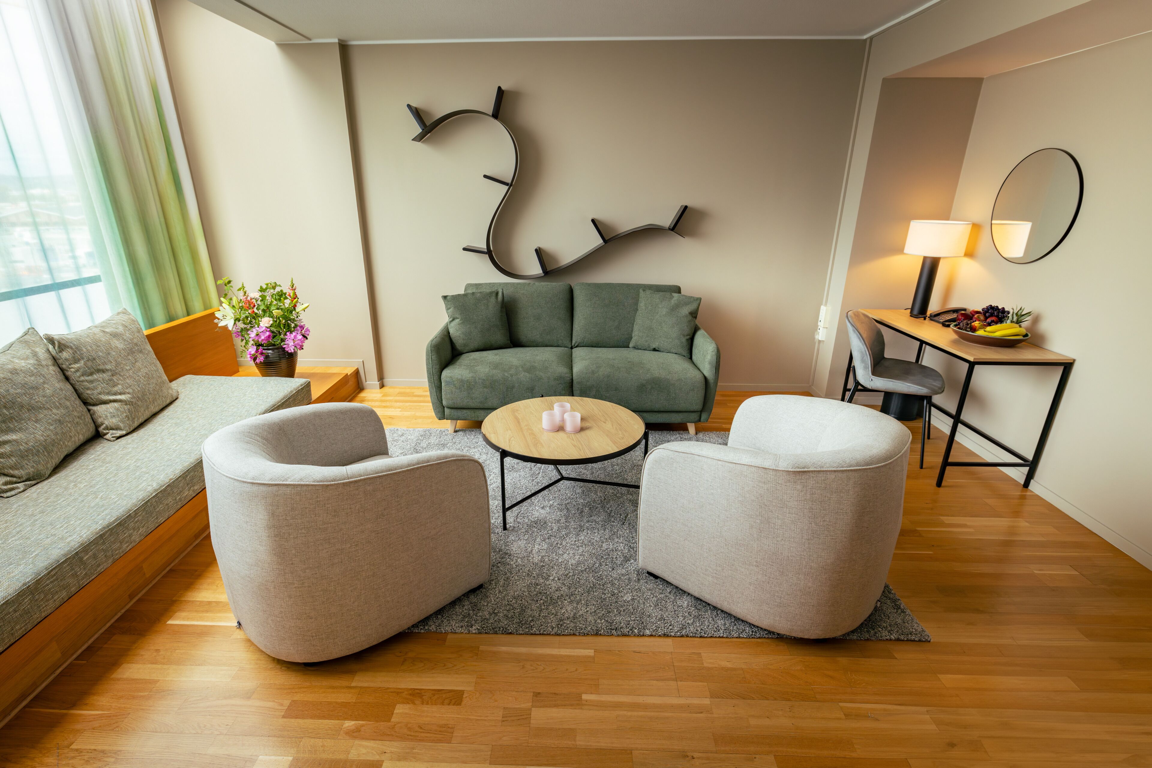 Uma sala de estar moderna com um sofá verde, duas poltronas, uma mesa de centro e uma mesa lateral com uma luminária e uma fruteira.