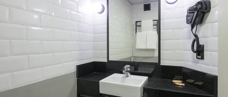 Um banheiro moderno com azulejos brancos tipo metrô, bancada preta, pia branca e secador de cabelo fixado na parede.