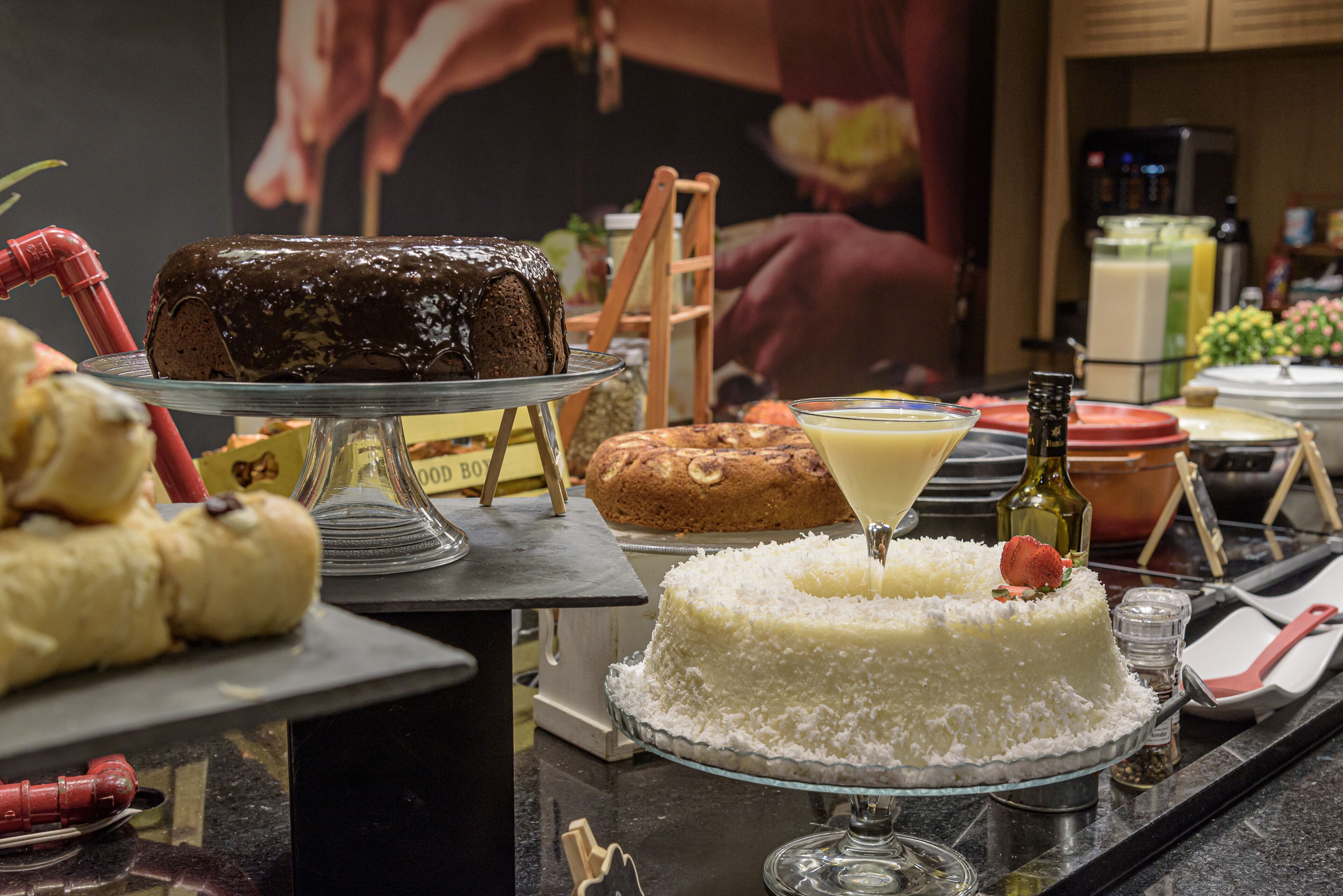 Diversos doces à mostra, incluindo um bolo de chocolate, um bolo branco com coco e um bolo coberto de frutas.