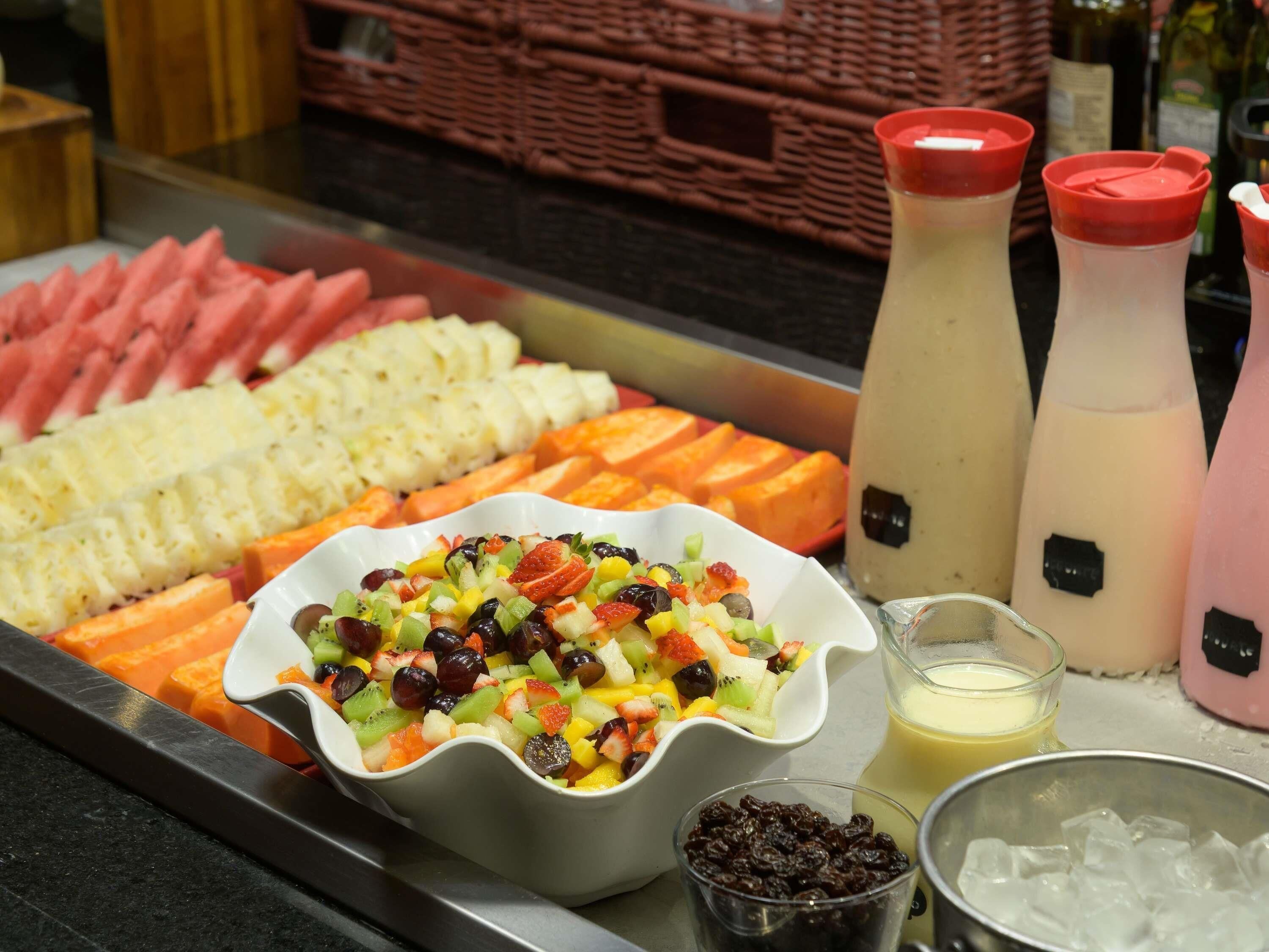 Buffet com diversos alimentos, incluindo carnes fatiadas, queijos e uma salada de frutas.
