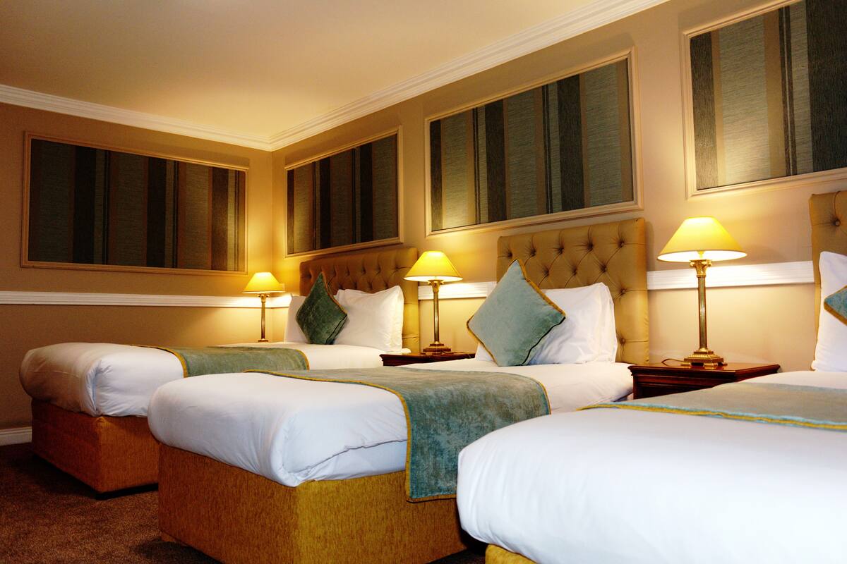 Quarto de hotel com duas camas, cada uma com cabeceira, mesas de cabeceira, luminárias e almofadas.