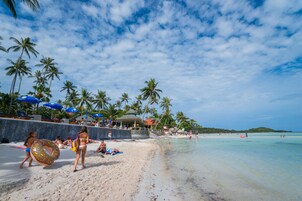 Na praia, areia branca, espreguiçadeiras, guarda-sóis 