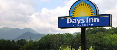 Placa da Days Inn com logotipo em forma de sol, ao fundo vegetação exuberante e montanhas.