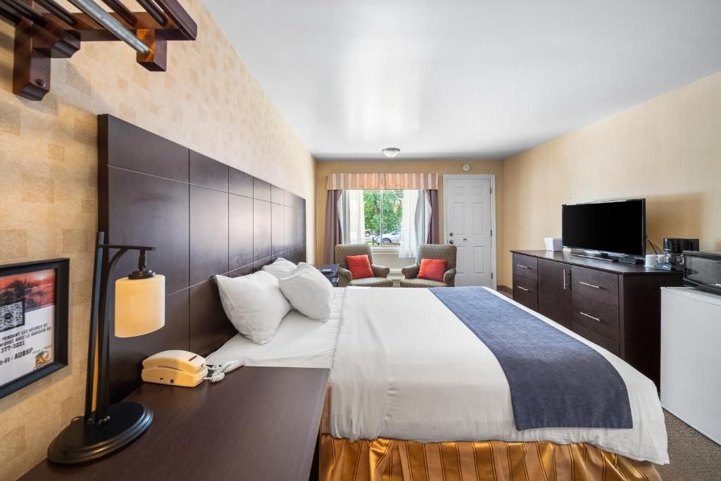 Quarto de hotel com cama, mesa de cabeceira, luminária, televisão e vista para o exterior.