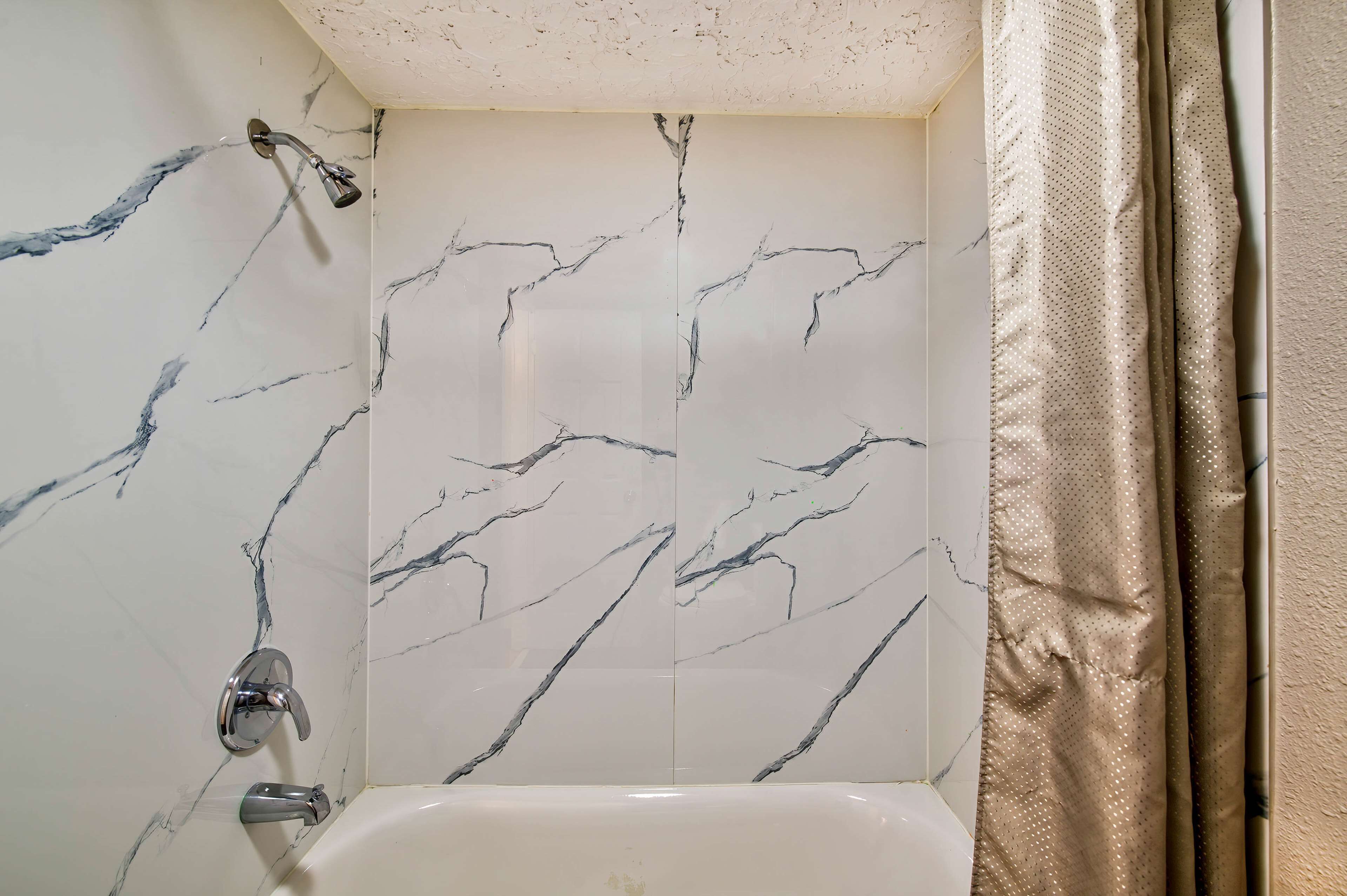 Casa de banho com azulejos de mármore branco com veios negros, uma banheira branca e um chuveiro com chuveiro manual.