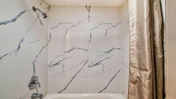 Casa de banho com azulejos de mármore branco com veios negros, uma banheira branca e um chuveiro com chuveiro manual.