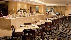 Um hall de hotel com balcão de recepção, várias mesas e cadeiras dispostas para refeições.