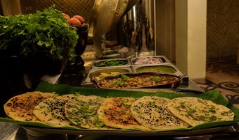 Buffet com diversos pratos, incluindo pães achatados e uma planta em vaso.