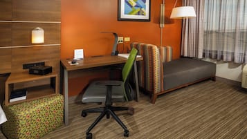 Quarto de hotel com escrivaninha, cadeira, cama e um quadro na parede.