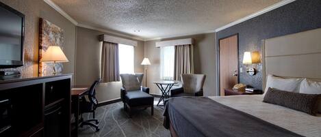 Quarto de hotel com cama, escrivaninha, cadeiras, televisão e abajur.
