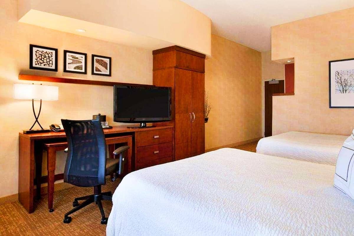 Quarto de hotel com cama, escrivaninha com televisão, cadeira e armário.