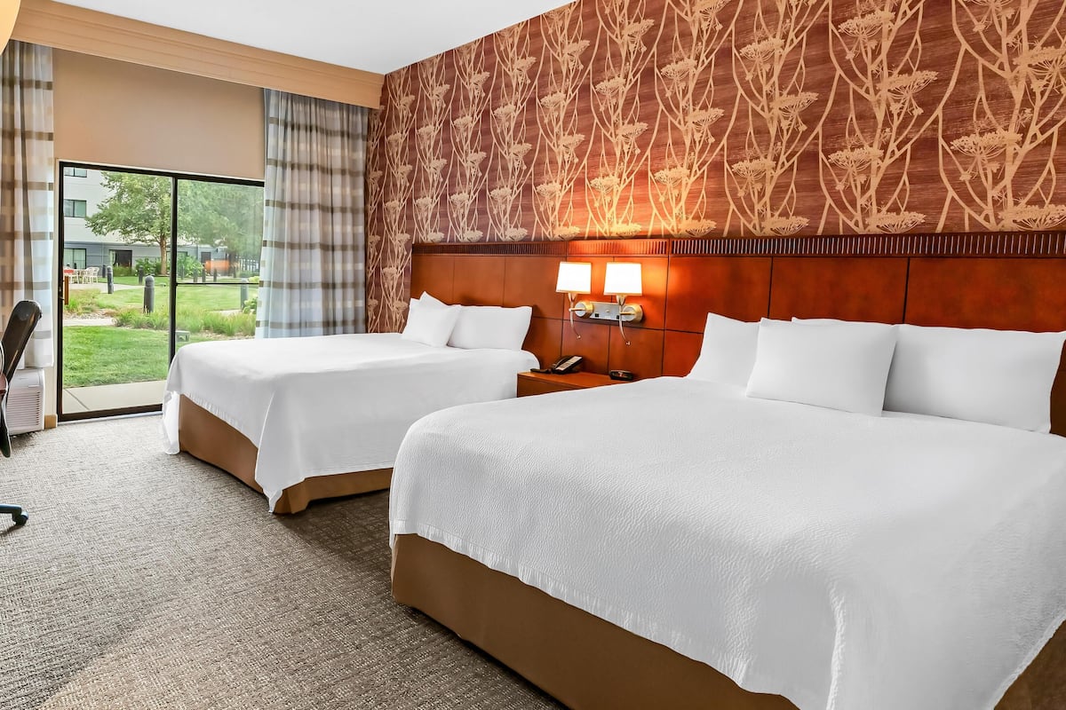 Quarto de hotel com duas camas, uma janela grande e parede estampada.