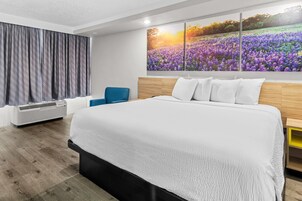 Quarto moderno com uma cama grande, uma cadeira azul, ar condicionado fixado na parede e uma grande obra de arte floral.
