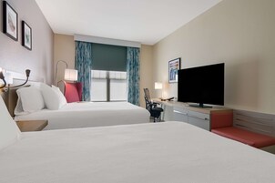 Quarto de hotel com duas camas, uma escrivaninha, uma televisão e uma janela com cortinas.