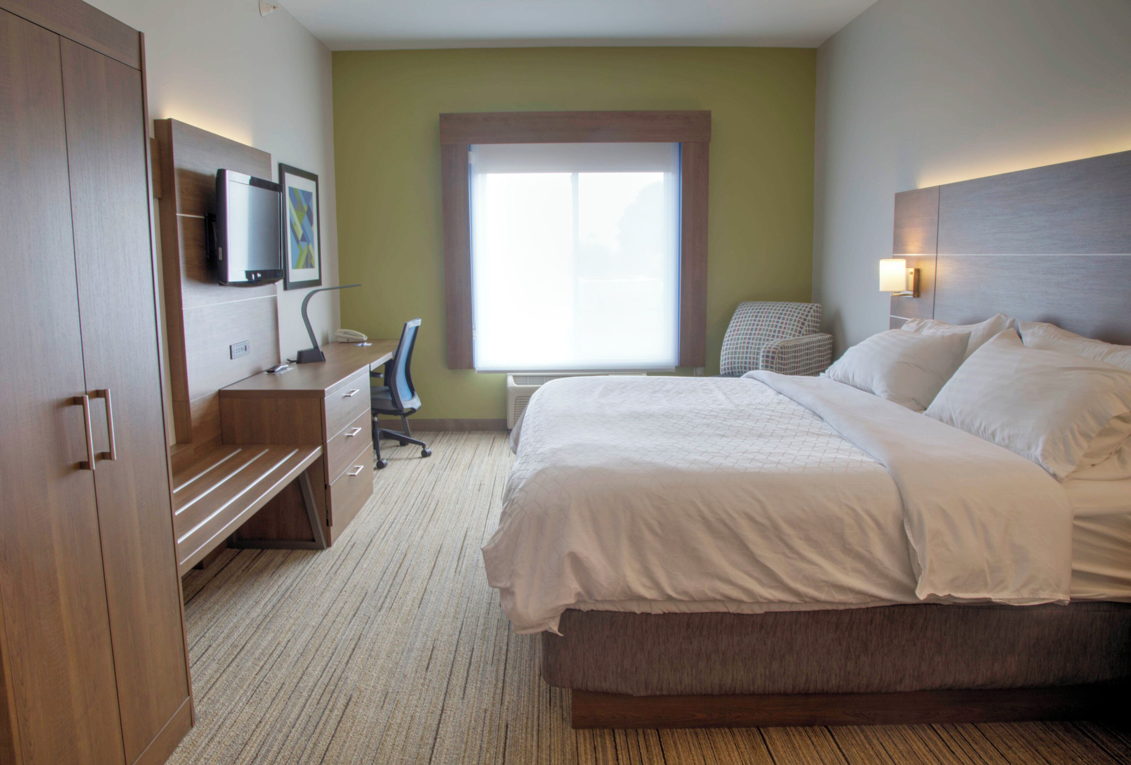 Quarto de hotel com cama, escrivaninha, cadeira e janela.