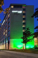 Edifício de hotel Courtyard com fachada verde iluminada, várias janelas e entrada visível.