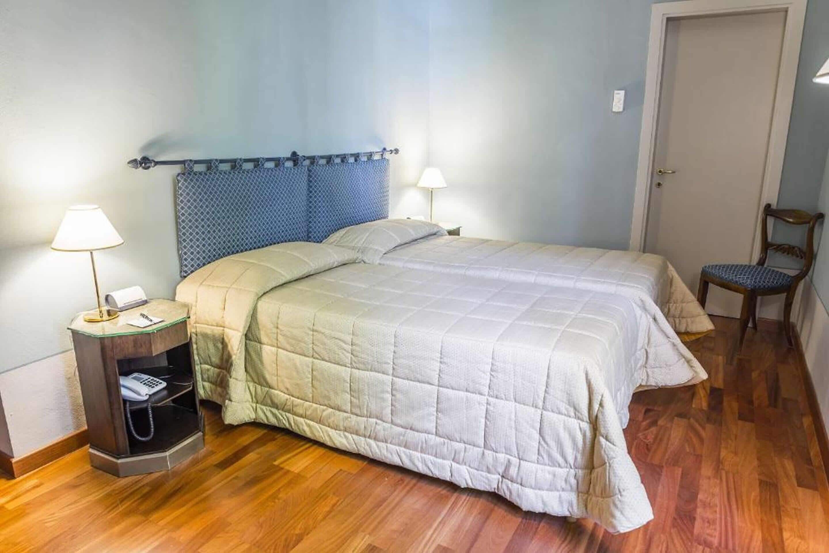 Quarto com cama, luminárias de cabeceira, uma cadeira e mesa de cabeceira com telefone.