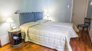 Quarto com cama, luminárias de cabeceira, uma cadeira e mesa de cabeceira com telefone.
