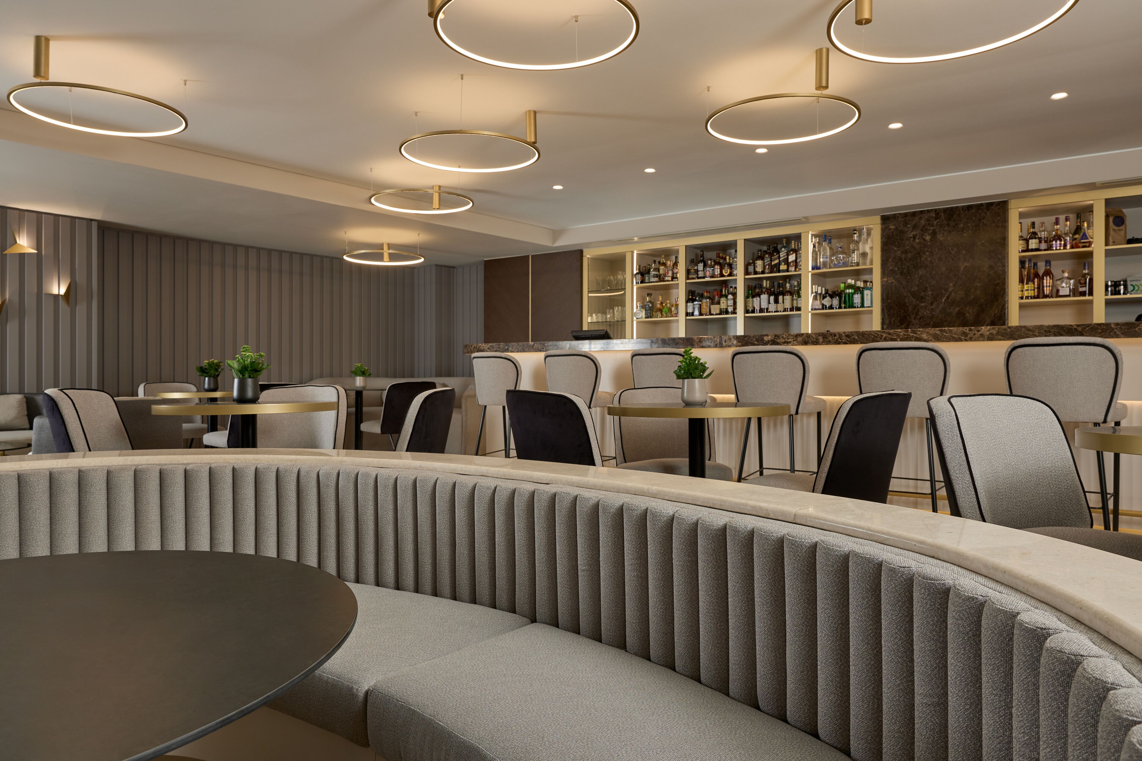 Um restaurante moderno com área de estar curva, iluminação pendente e um bar com prateleiras de garrafas.