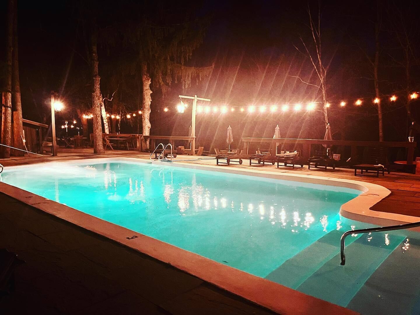 Piscina à noite com espreguiçadeiras e luzes de fada.