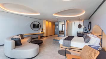 Quarto de hotel moderno com sofá curvo, cama com cabeceira, espelho redondo e uma pequena mesa.
