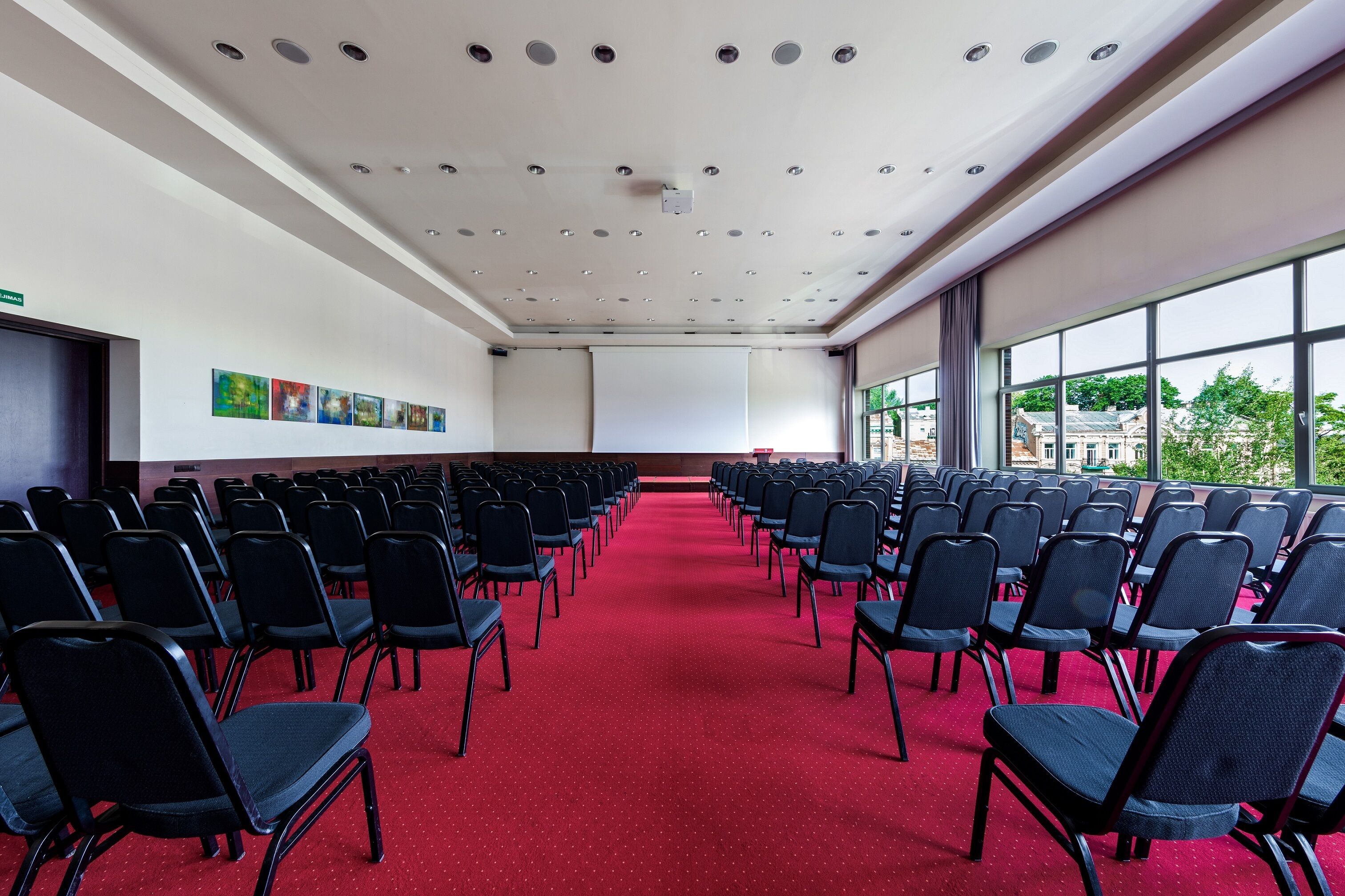 Uma sala de conferência com fileiras de cadeiras, um tapete vermelho e uma tela de projetor.