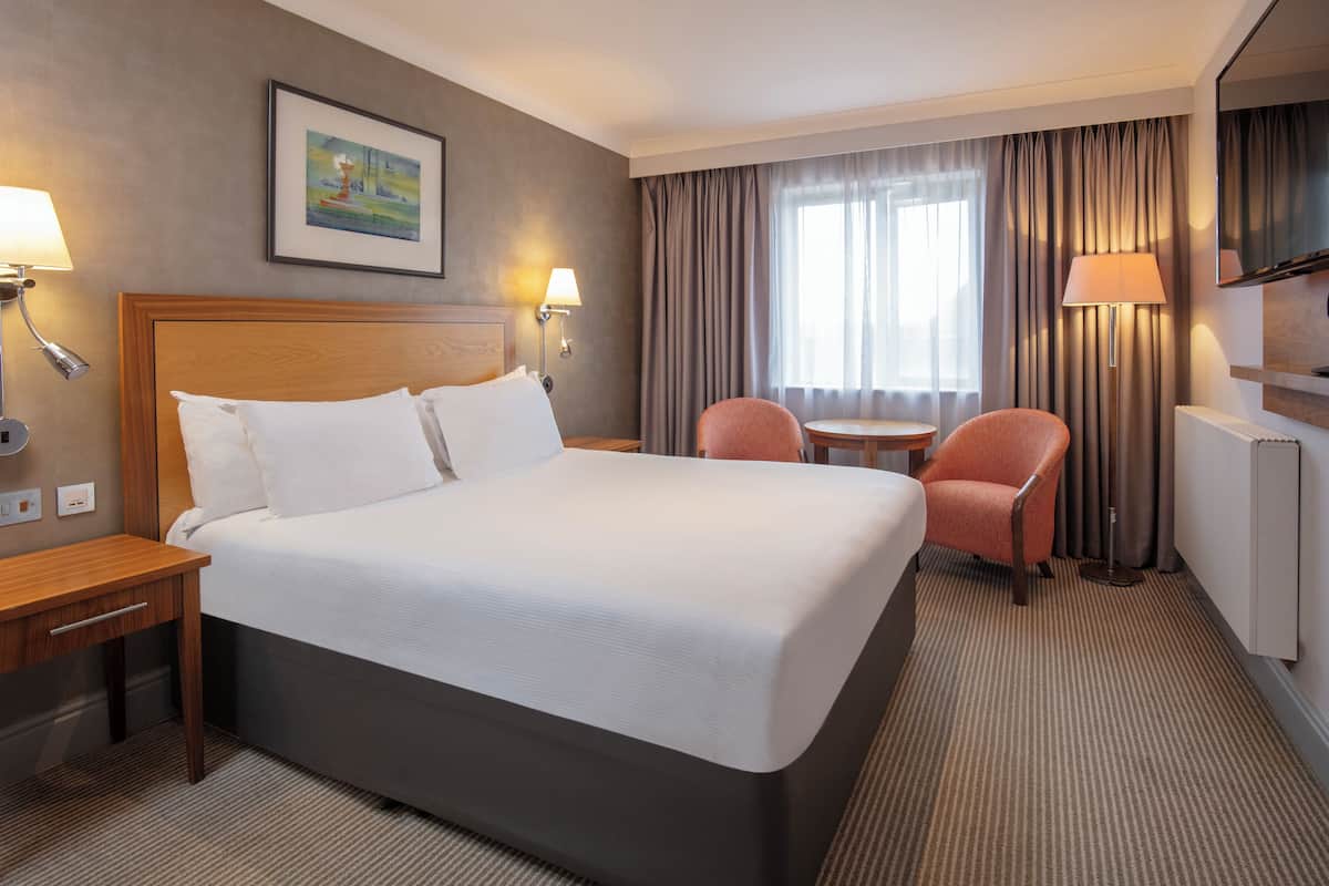 Quarto de hotel com uma cama grande, uma escrivaninha, uma cadeira, uma mesa pequena e uma televisão.