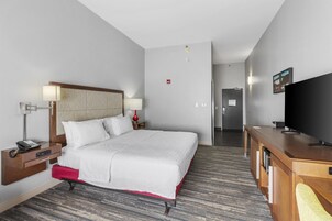 Quarto de hotel com cama, mesas de cabeceira, escrivaninha, televisão e piso coberto de carpete.