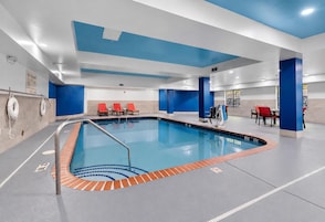 Piscina interior com esquema de cores azul e branco, cadeira de salva-vidas e escada para piscina.