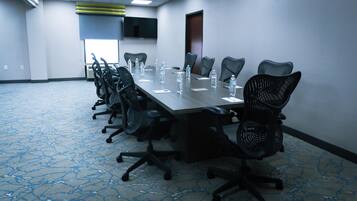 Sala de conferências com uma mesa comprida, várias cadeiras, garrafas de água e uma tela de televisão na parede.