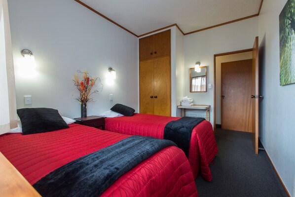 Quarto de hotel com duas camas, uma escrivaninha, um espelho e uma porta.