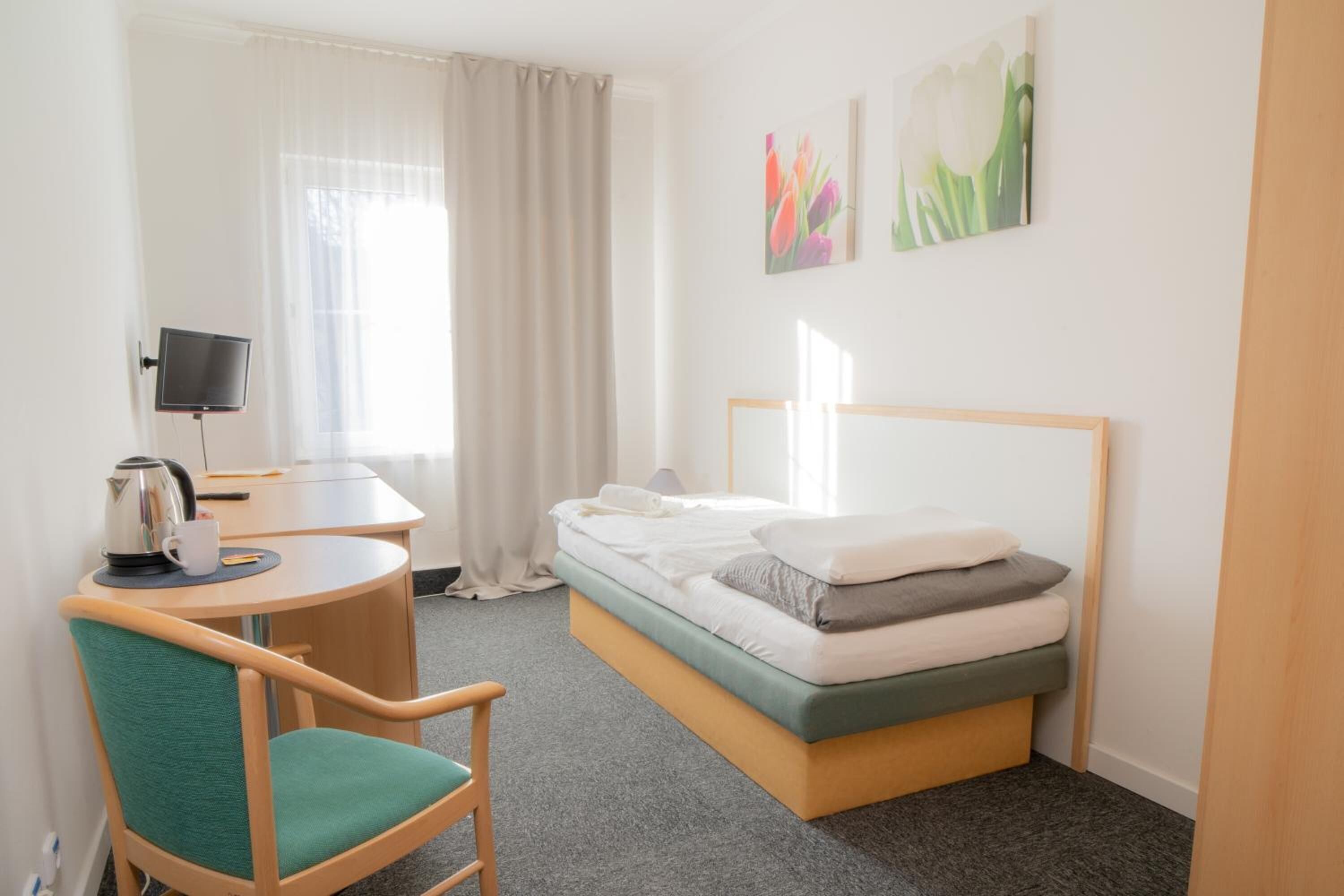 Quarto de hotel com cama, escrivaninha, cadeira, chaleira e televisão de tela plana.