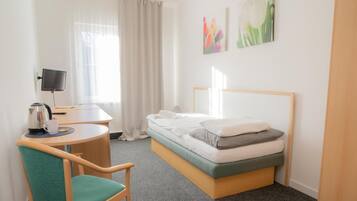 Quarto de hotel com cama, escrivaninha, cadeira, chaleira e televisão de tela plana.