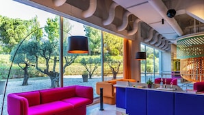 Um interior moderno com um sofá vermelho, uma área de cozinha azul e amplas janelas com vista para árvores e vegetação.