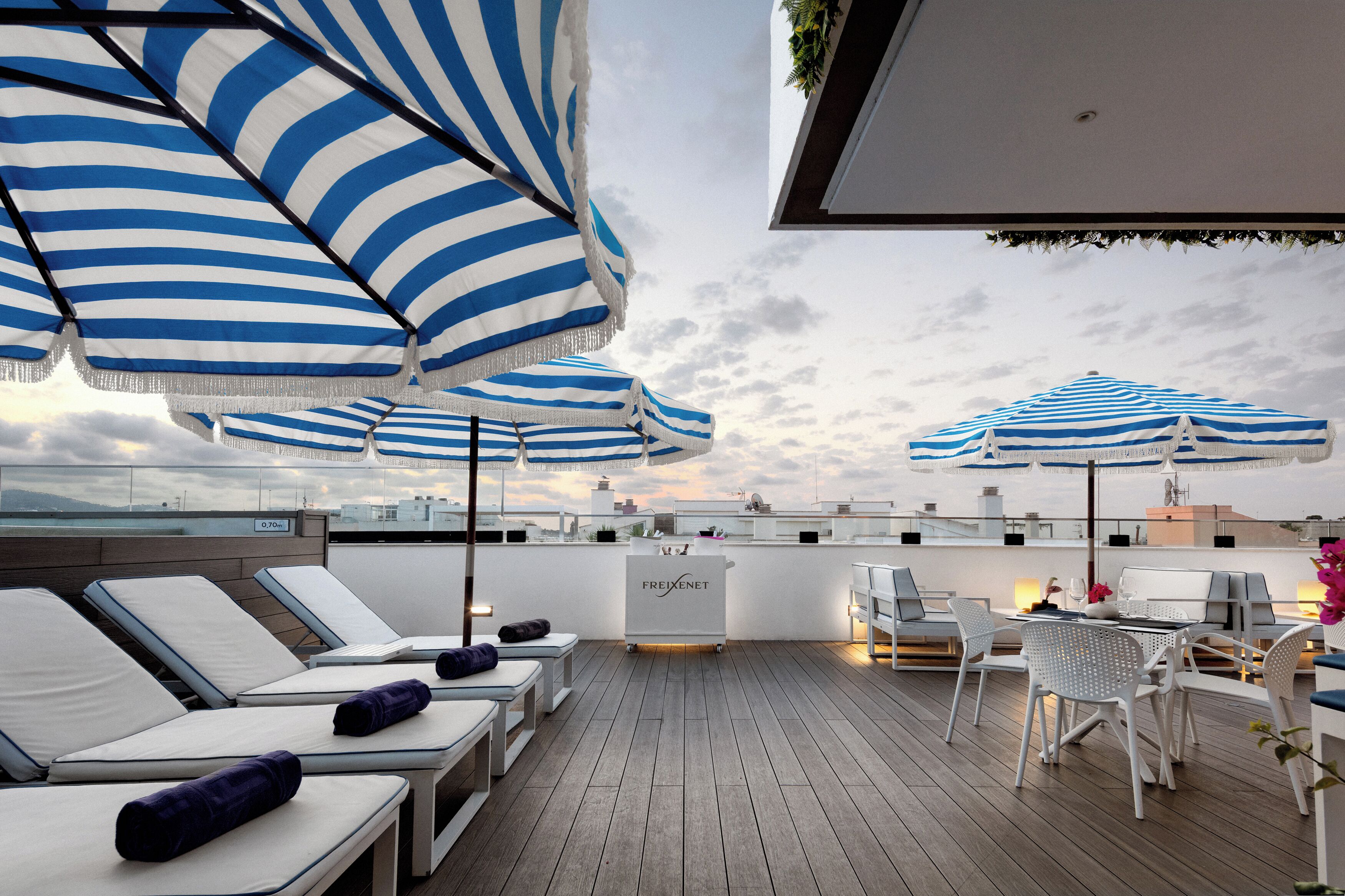 Área de lounge no terraço, com guarda-sóis listrados, espreguiçadeiras e um bar.