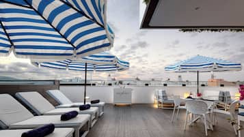 Área de lounge no terraço, com guarda-sóis listrados, espreguiçadeiras e um bar.