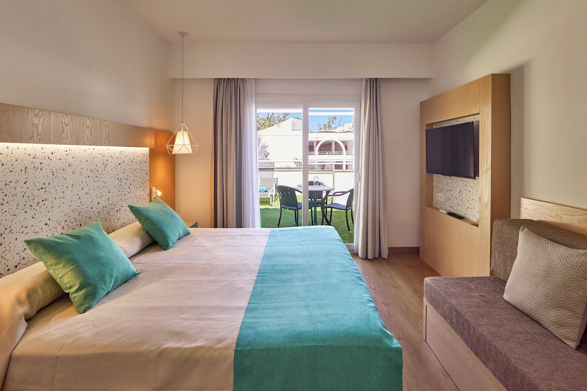 Quarto de hotel com uma cama grande, um sofá, uma TV e uma varanda com móveis de exterior.
