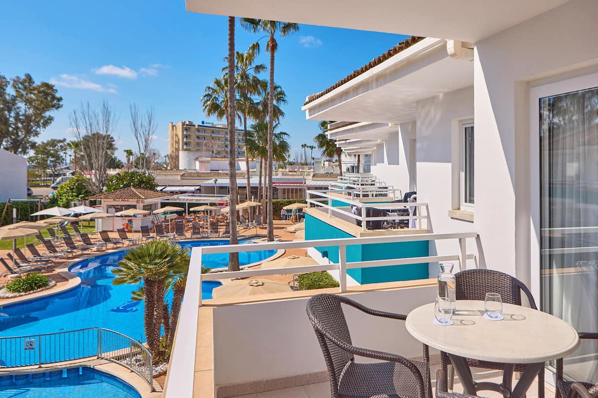Varanda com vista para uma piscina, cadeiras de descanso e uma mesa com copos.